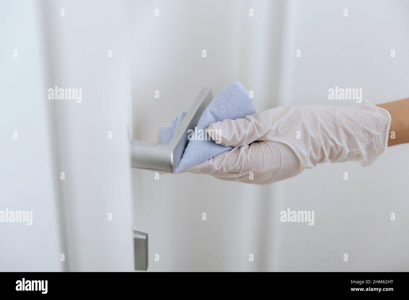 Cleaning door handle with blue wipe in white gloves. Woman hand using ...
