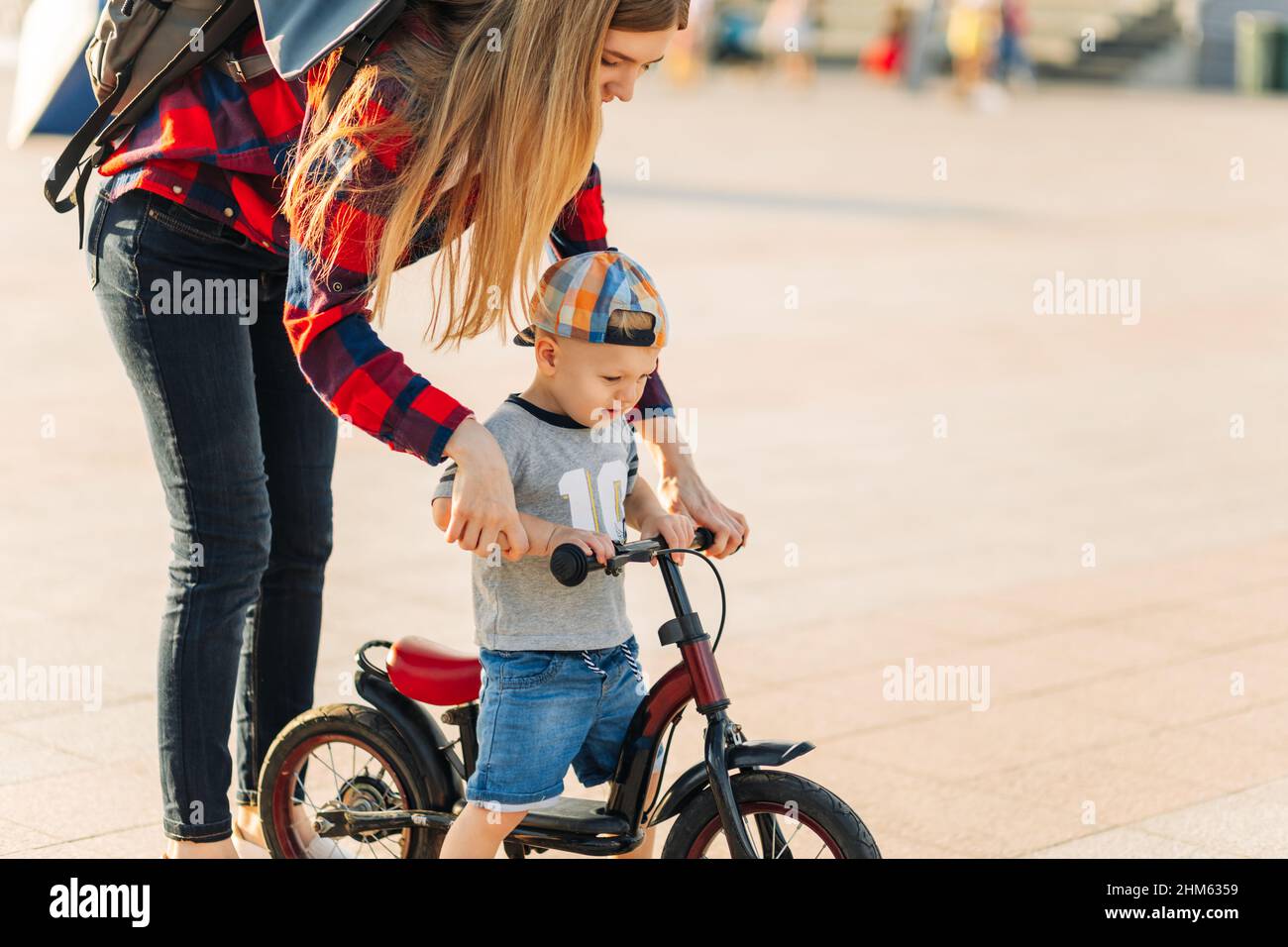 little boy is learning to ride a bike with his Mom in the park. Happy ...