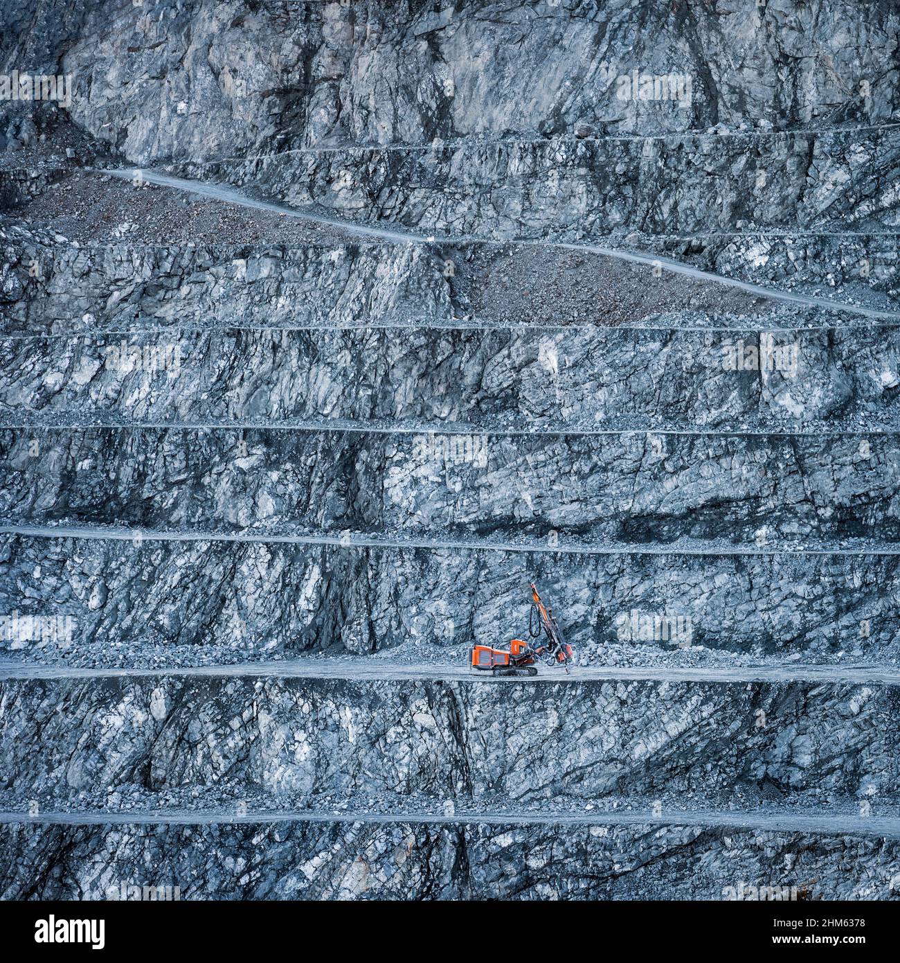 Stepped wall of diabase stone quarry with red drilling rig on a bench ...