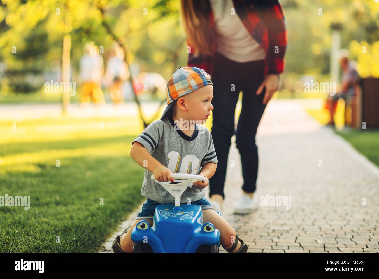 Happy cute boy ride a child's car, walking in the park with mom, mom ...