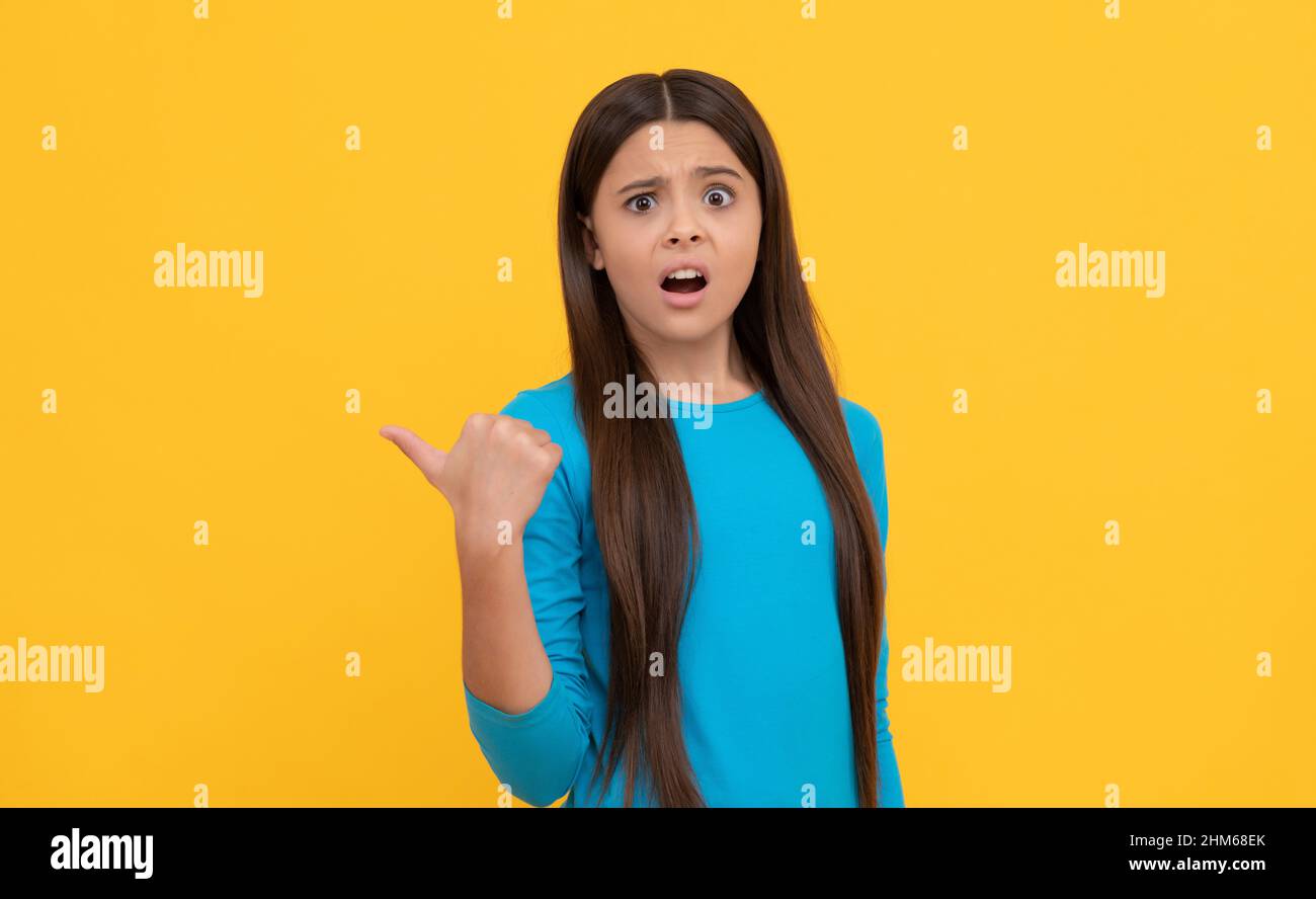 confused kid with long hair point finger on copy space on yellow ...