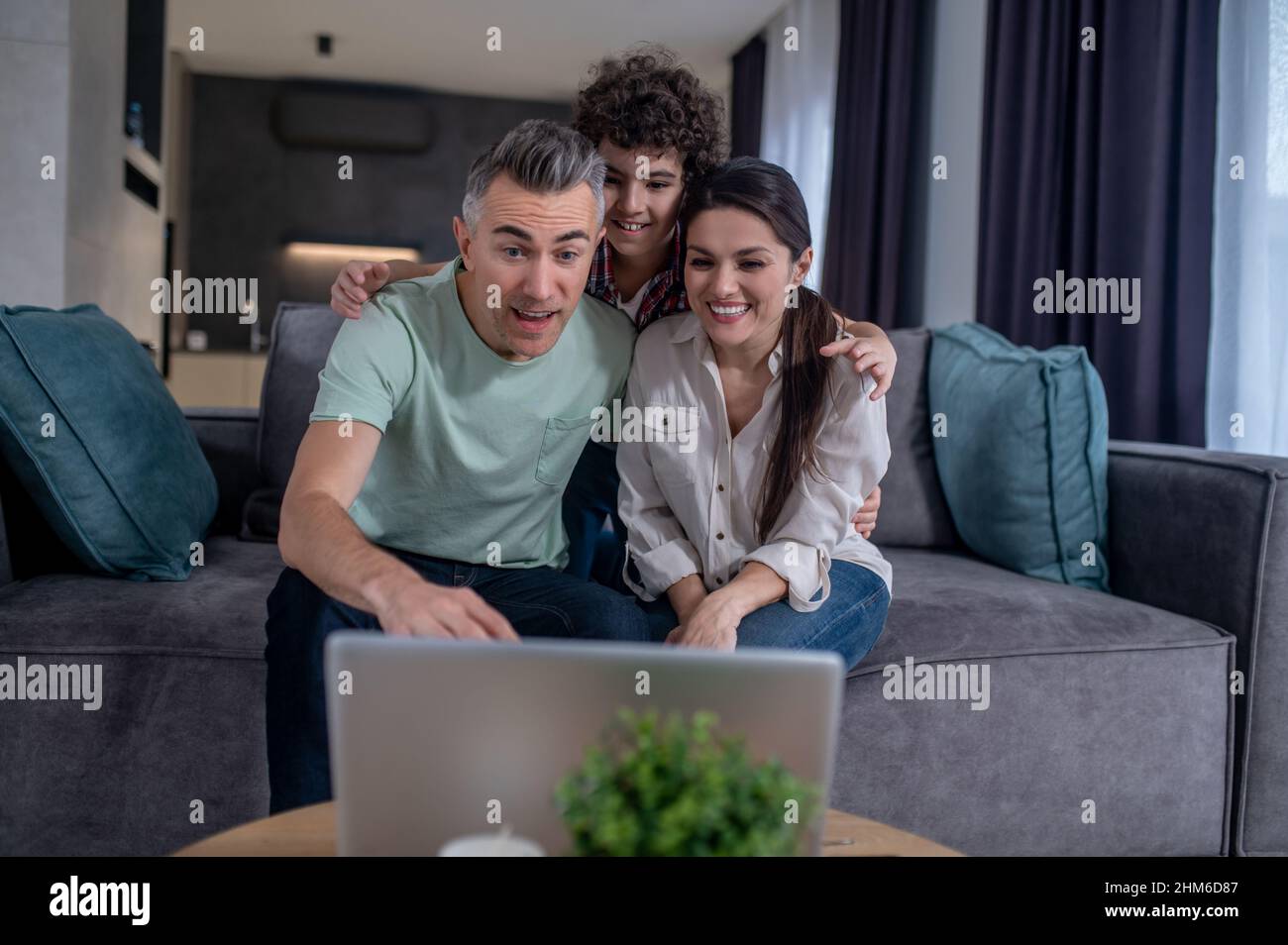 Boy hugging parents looking at laptop sitting on sofa Stock Photo - Alamy