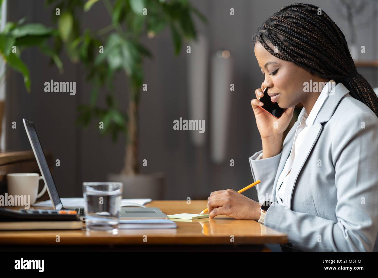 Serious afro woman in suit talking on mobile phone and writing down ...