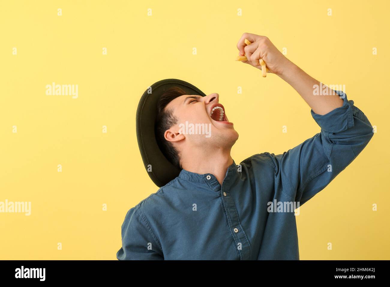 Emotional young man eating french fries on yellow background Stock ...