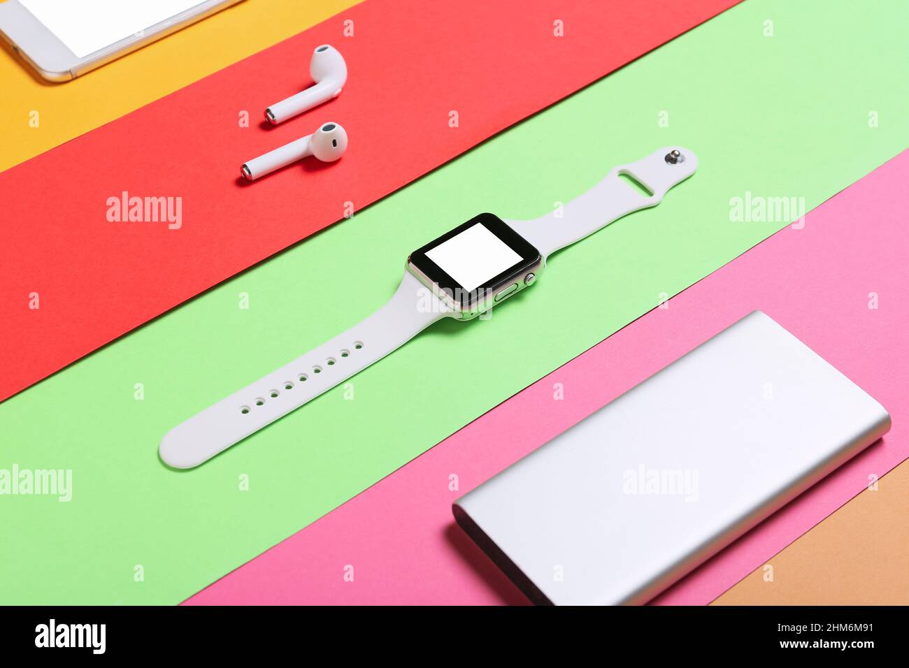 Modern power bank, smart watch and earphones on color background ...