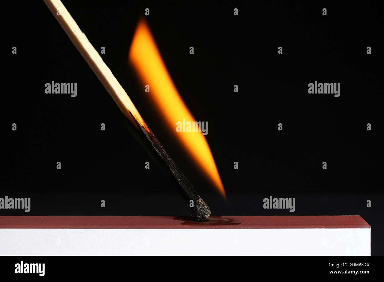 Burning match and surface of matchbox on black background, closeup ...
