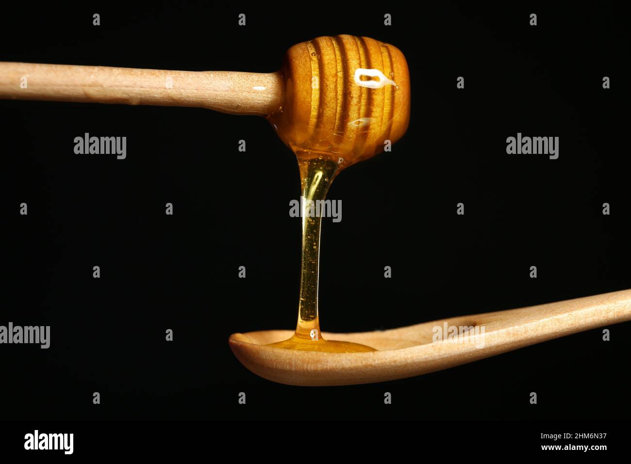 Honey dripping from dipper into wooden spoon on black background ...