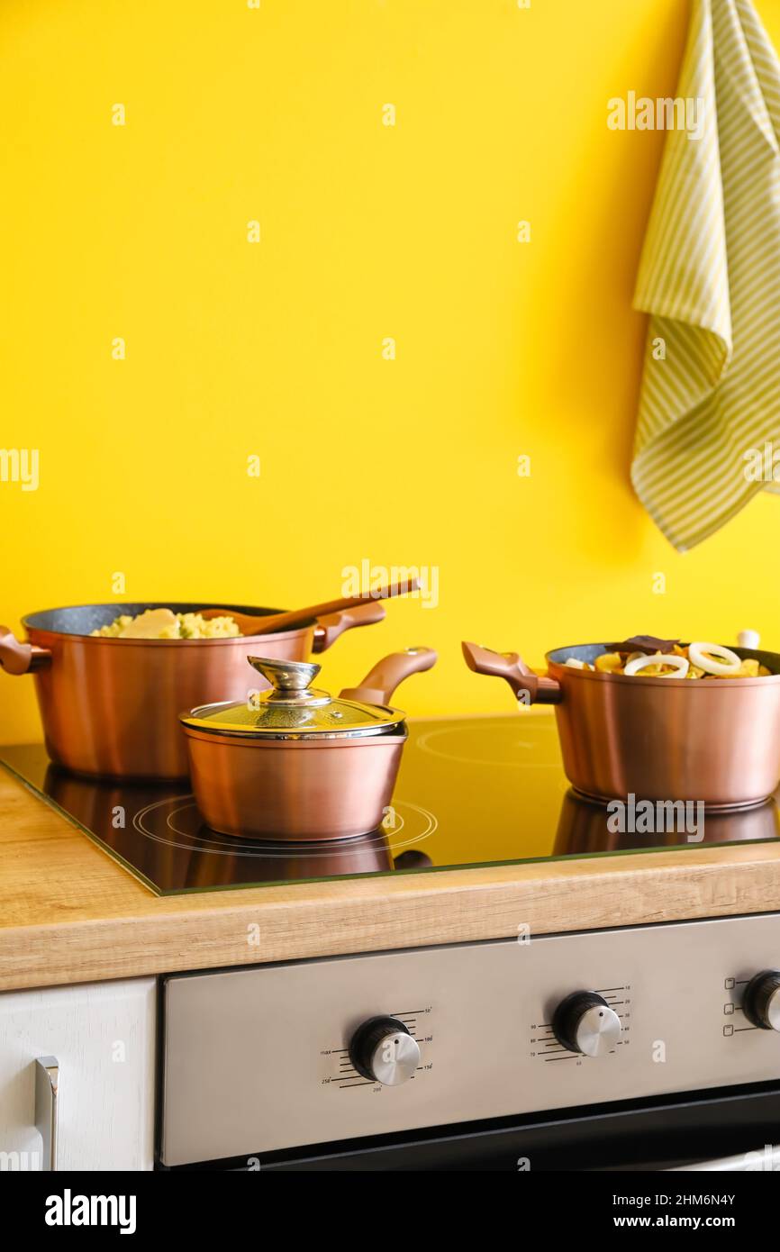Cooking pots with prepared food on stove near color wall Stock Photo ...