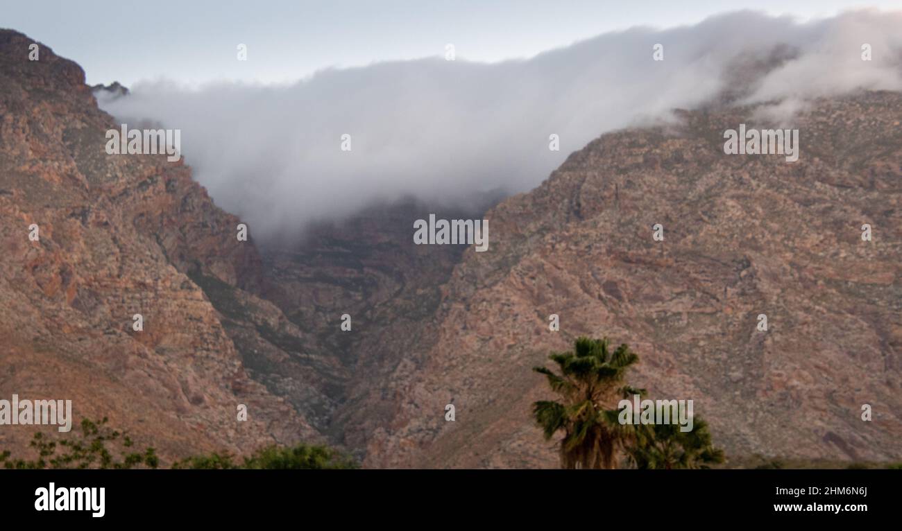 Misty clouds build up at the top of a mountain and blow down a natural ...