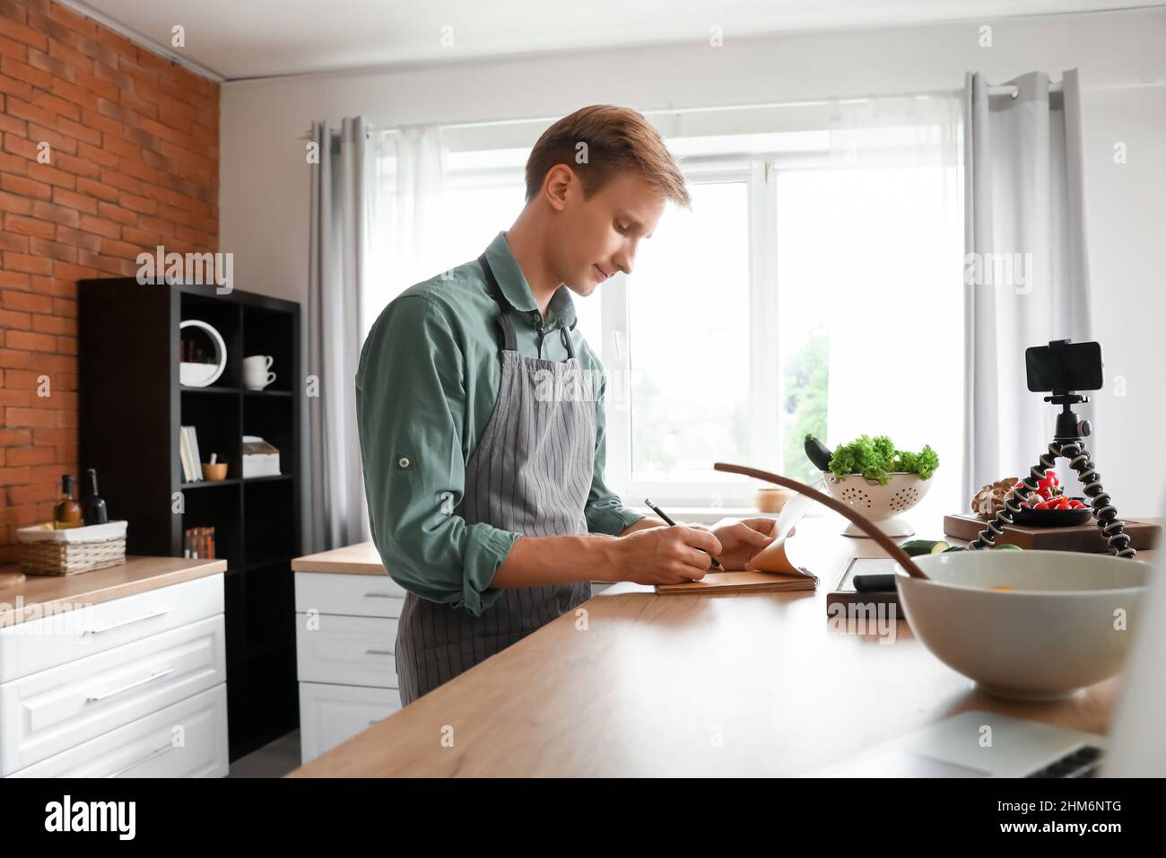 Young man making notes from cooking video tutorial in kitchen Stock ...