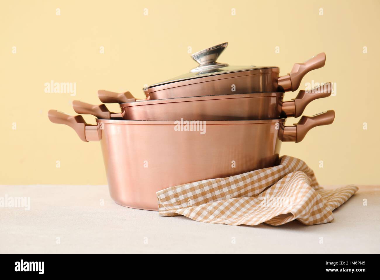 Shiny cooking pots with napkin on table against yellow background Stock ...