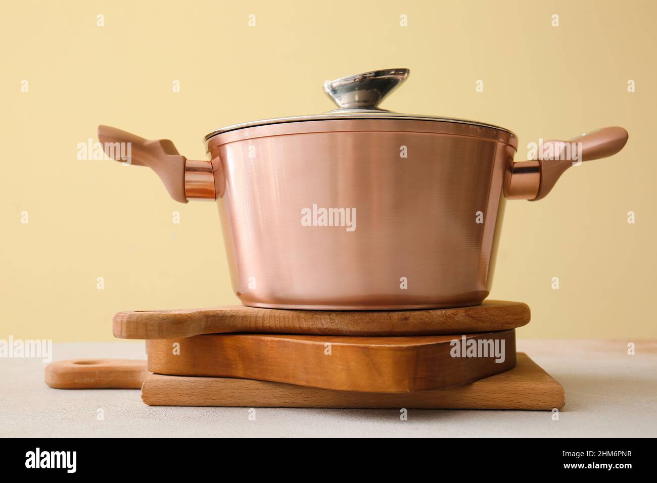 Shiny cooking pot with cutting boards on table against yellow ...