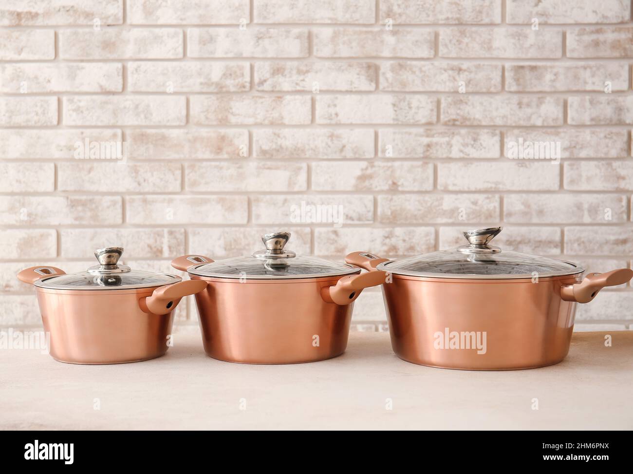 Shiny cooking pots on table against brick background Stock Photo - Alamy
