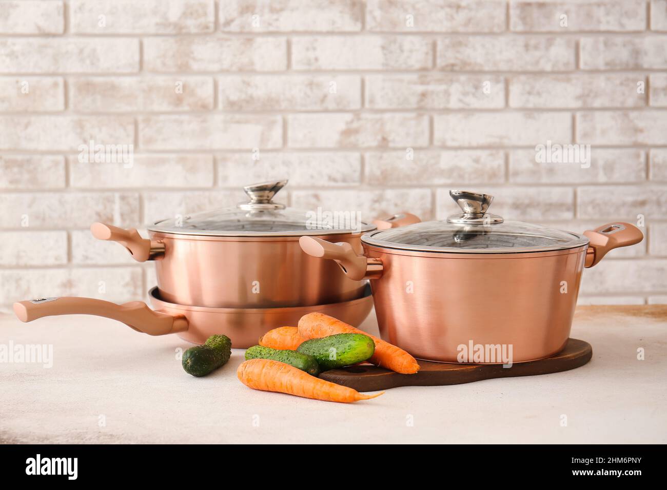 Shiny cooking pots with vegetables on table against brick background ...