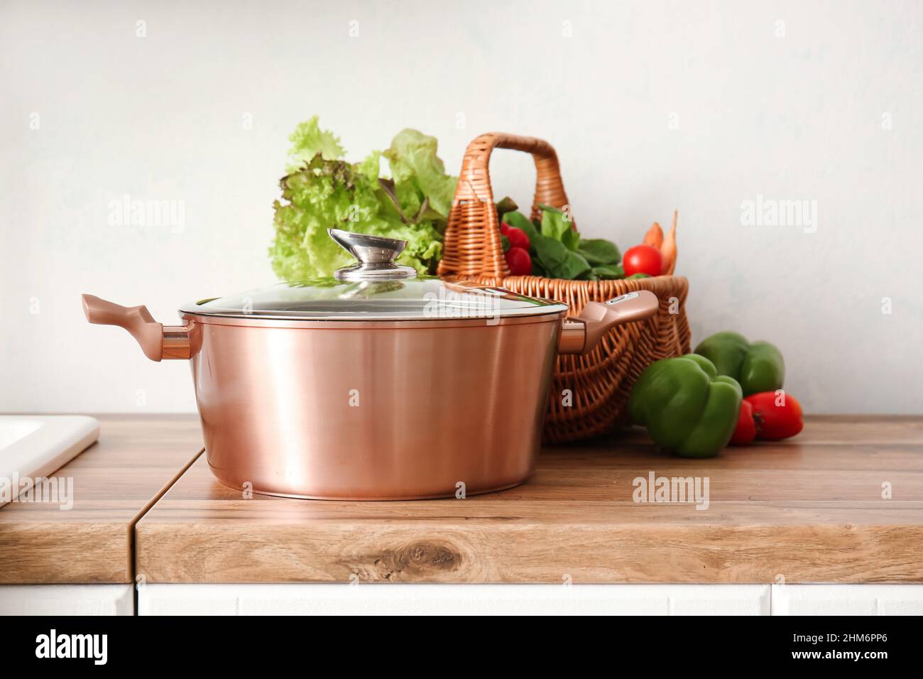 Shiny cooking pot and basket with fresh vegetables on counter near ...