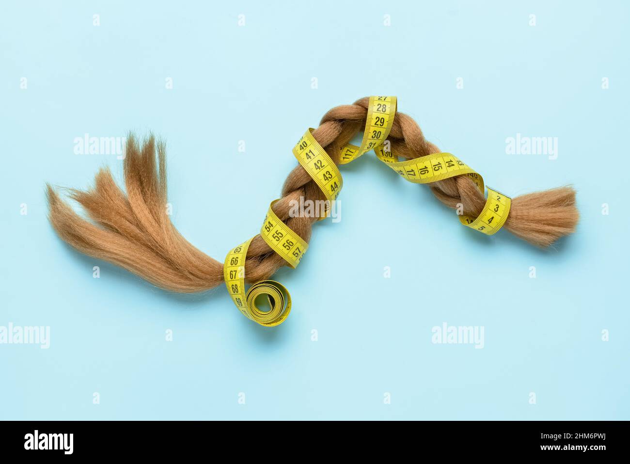 Braided red hair for donation with measuring tape on blue background ...