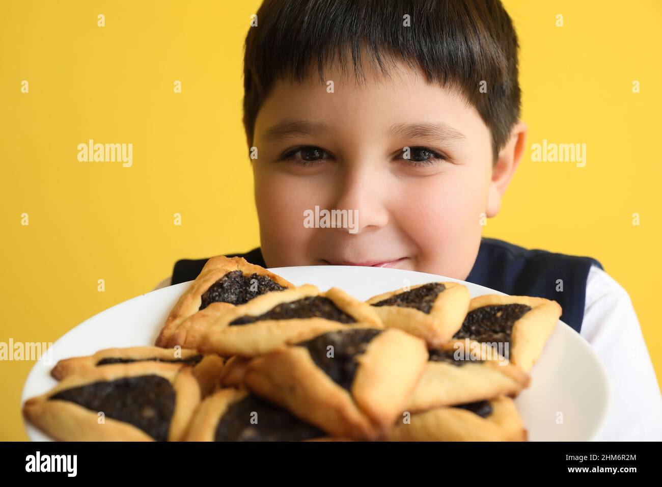 Little Jewish boy with tasty Hamantaschen for Purim holiday on color ...