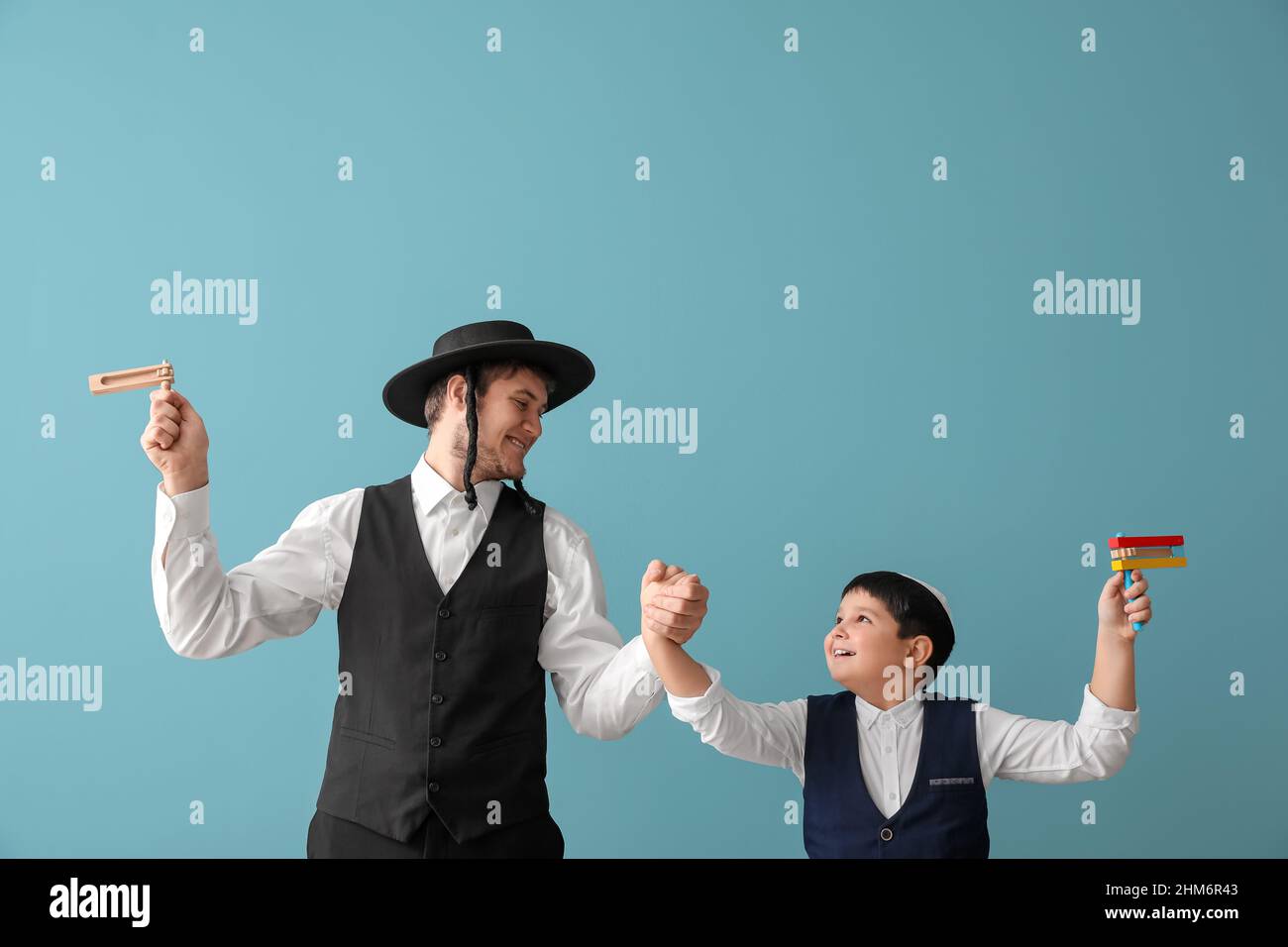 Happy Jewish man and boy with graggers for Purim holiday on grey ...