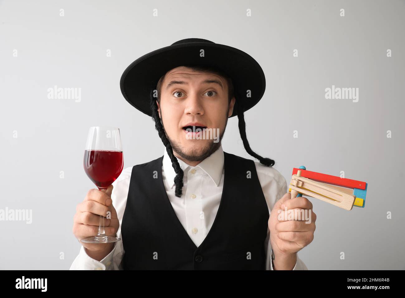 Surprised Jewish man with glass of wine and gragger for Purim holiday ...