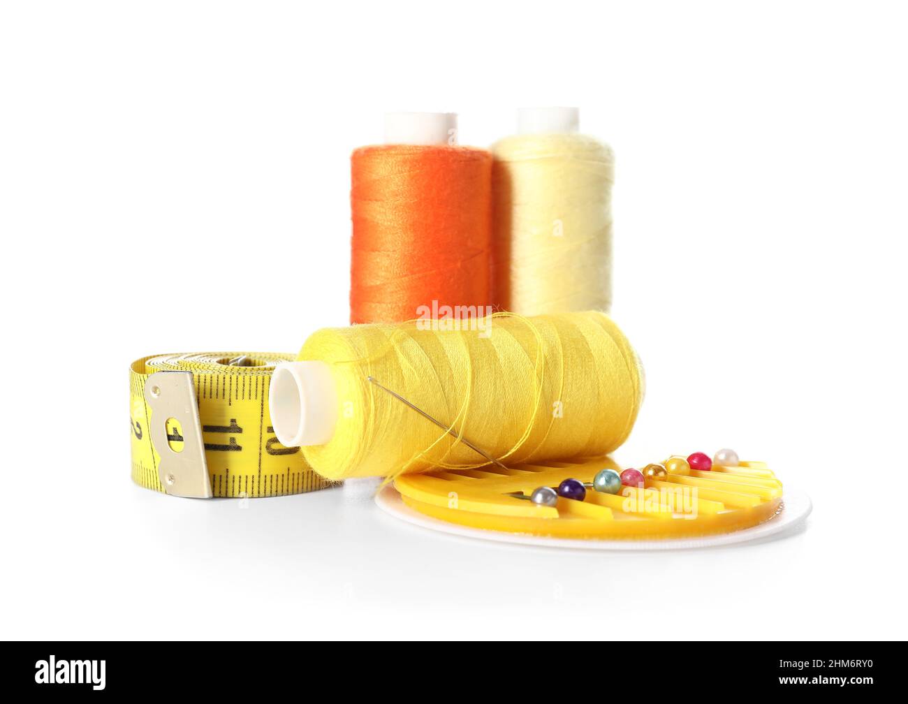 Different sewing threads with needles and measuring tape on white ...