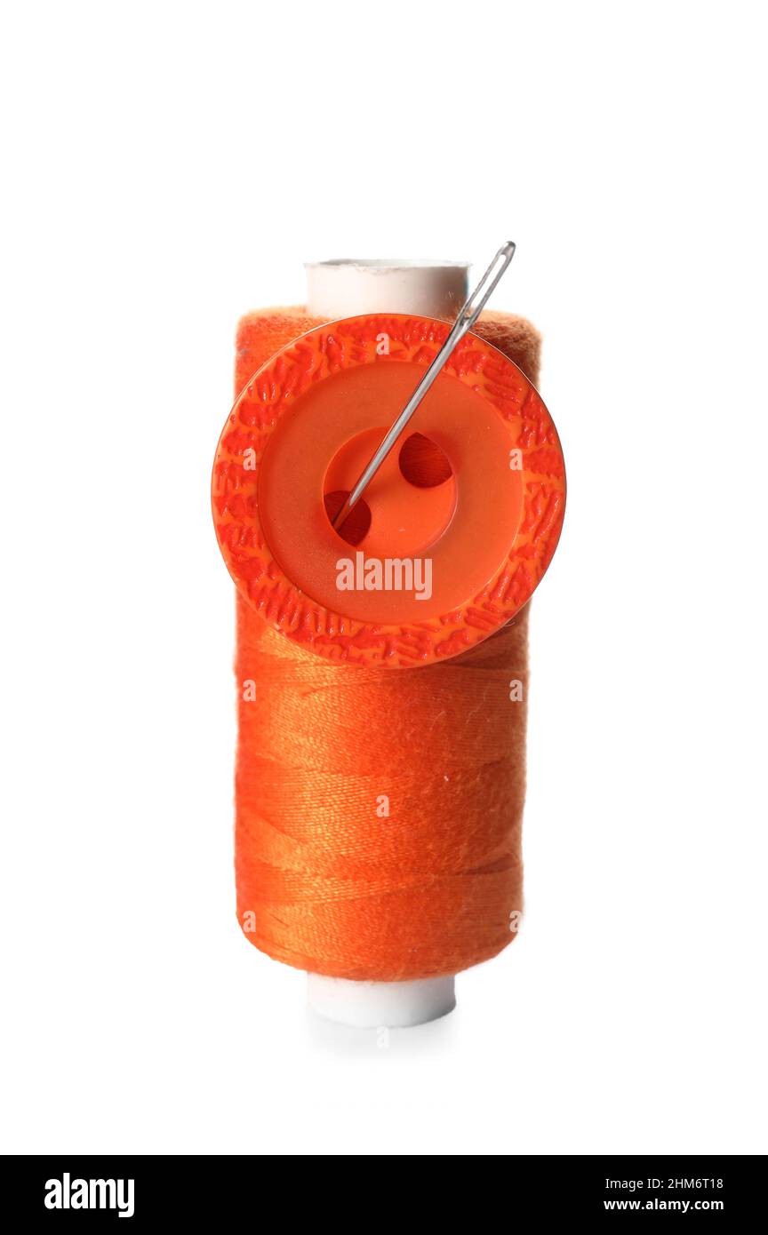 Orange sewing thread spool with needle and button on white background ...