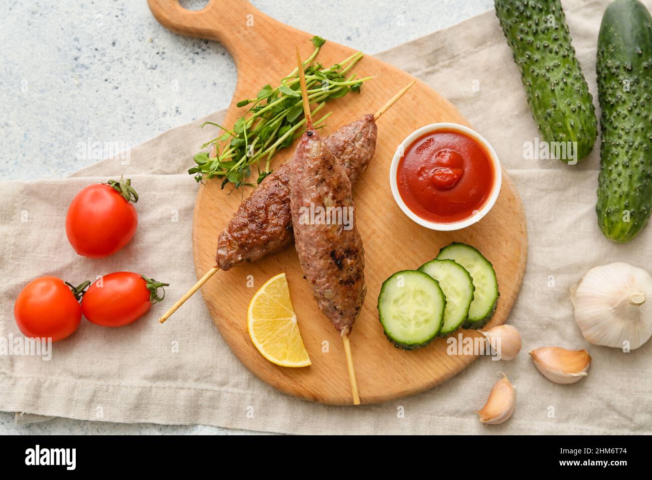 Wooden board of skewers with tasty lula kebab and vegetables on table ...