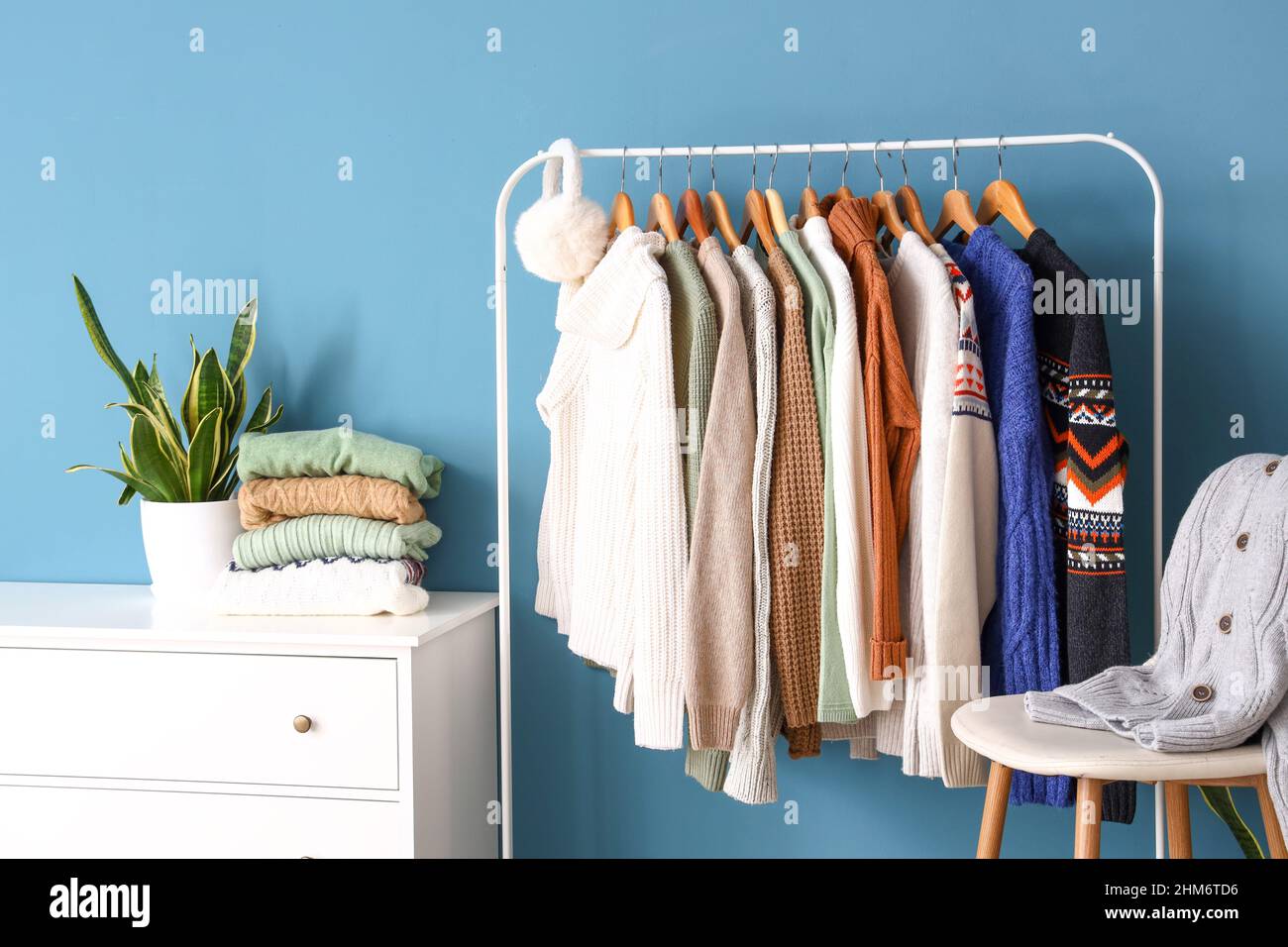 Rack with stylish sweaters, chest of drawers and chair near color wall ...