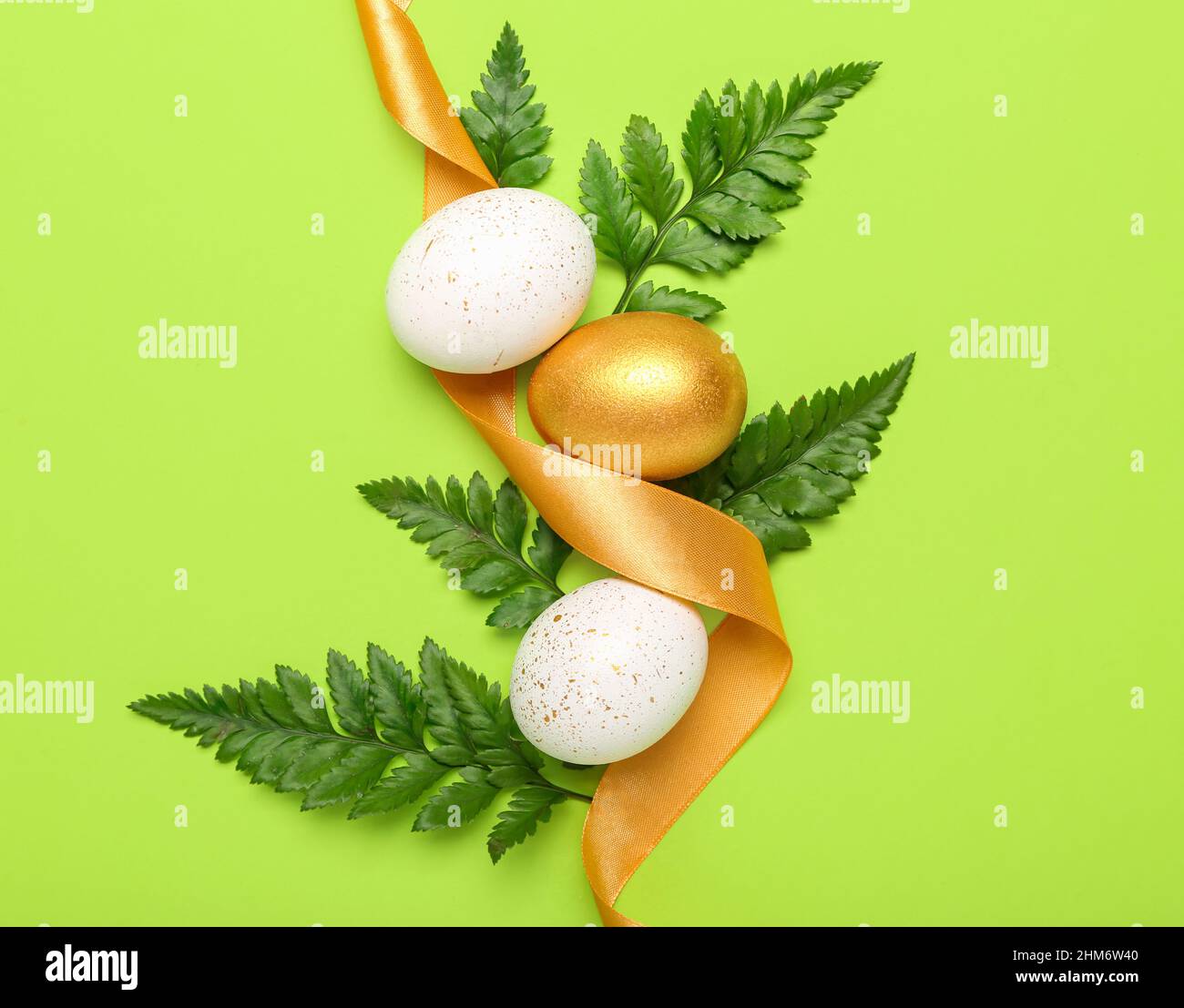 Composition with beautiful Easter eggs, ribbon and fern leaves on green ...