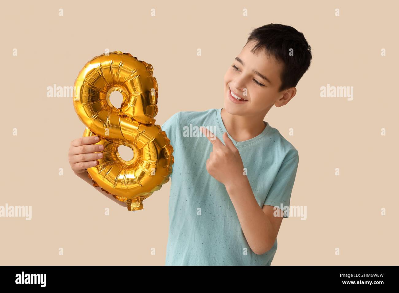 Little boy pointing at balloon in shape of figure 8 on beige background ...
