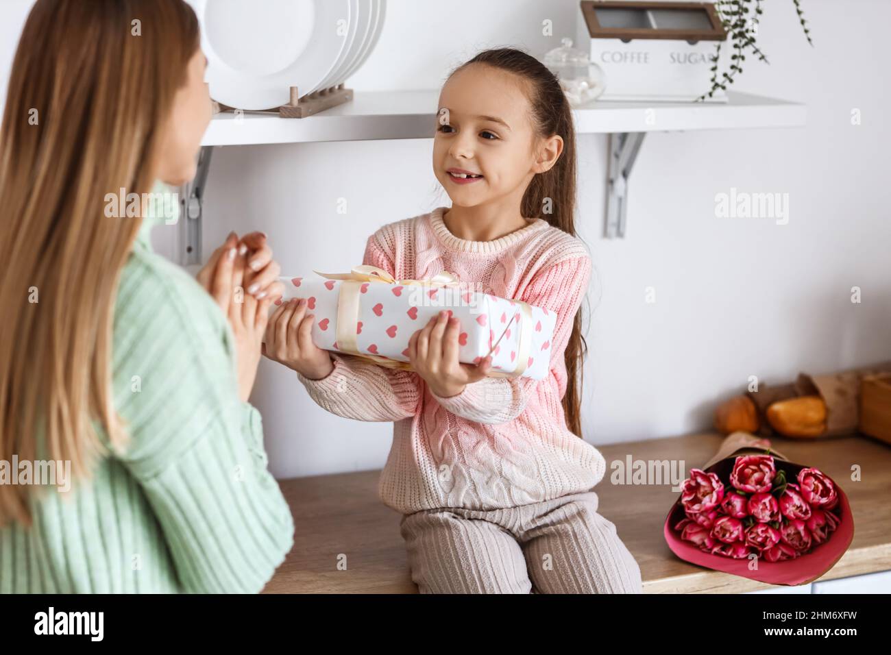 Little girl greeting her mother with gift in kitchen on International ...