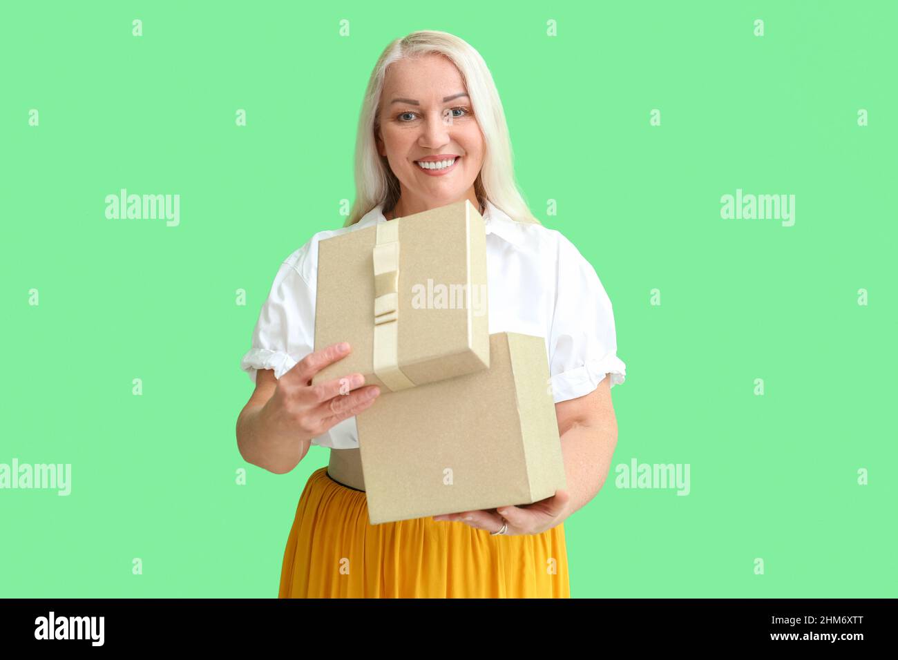 Smiling mature woman opening gift box on green background ...