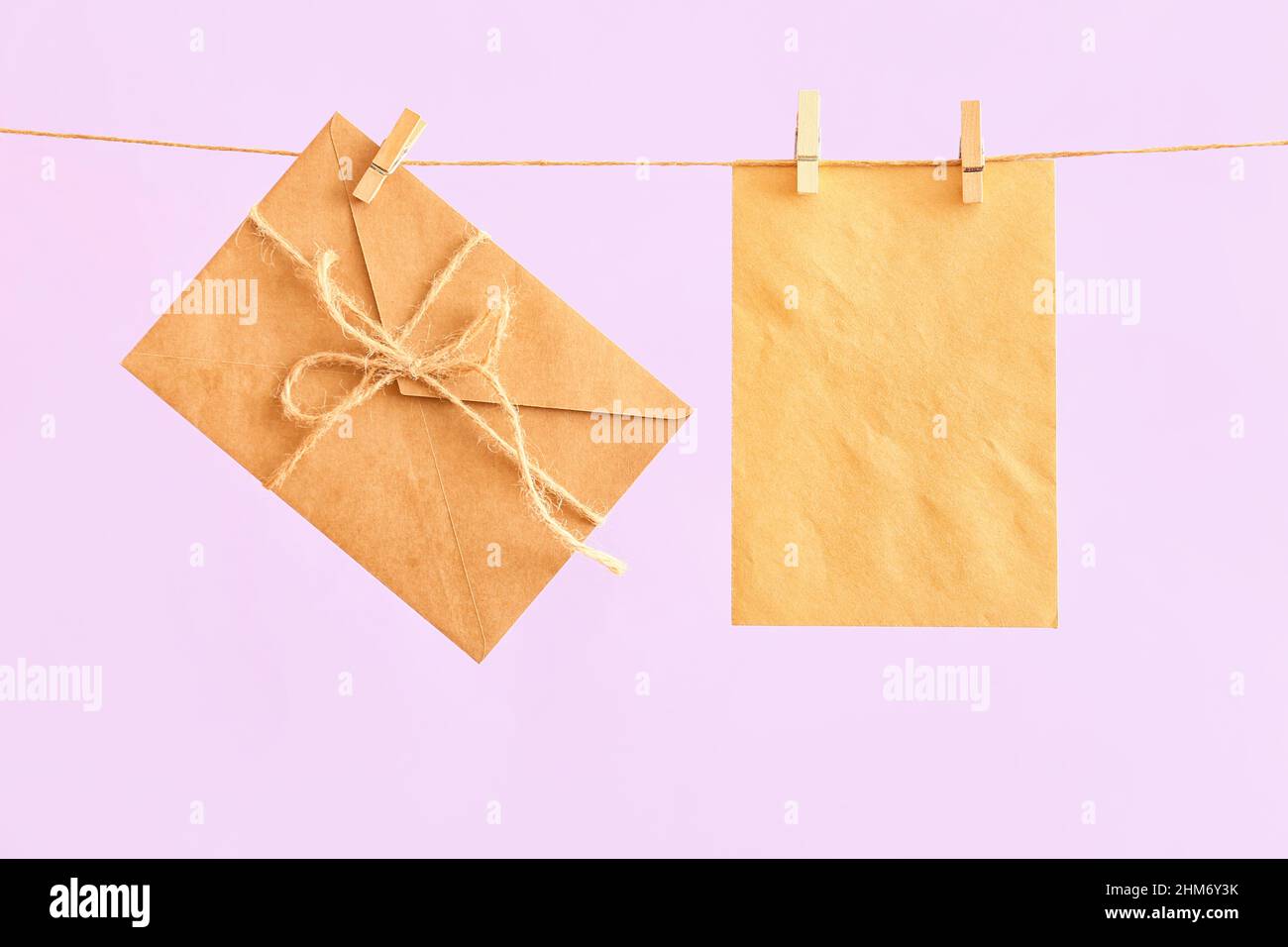 Blank card and envelope hanging on rope against color background ...