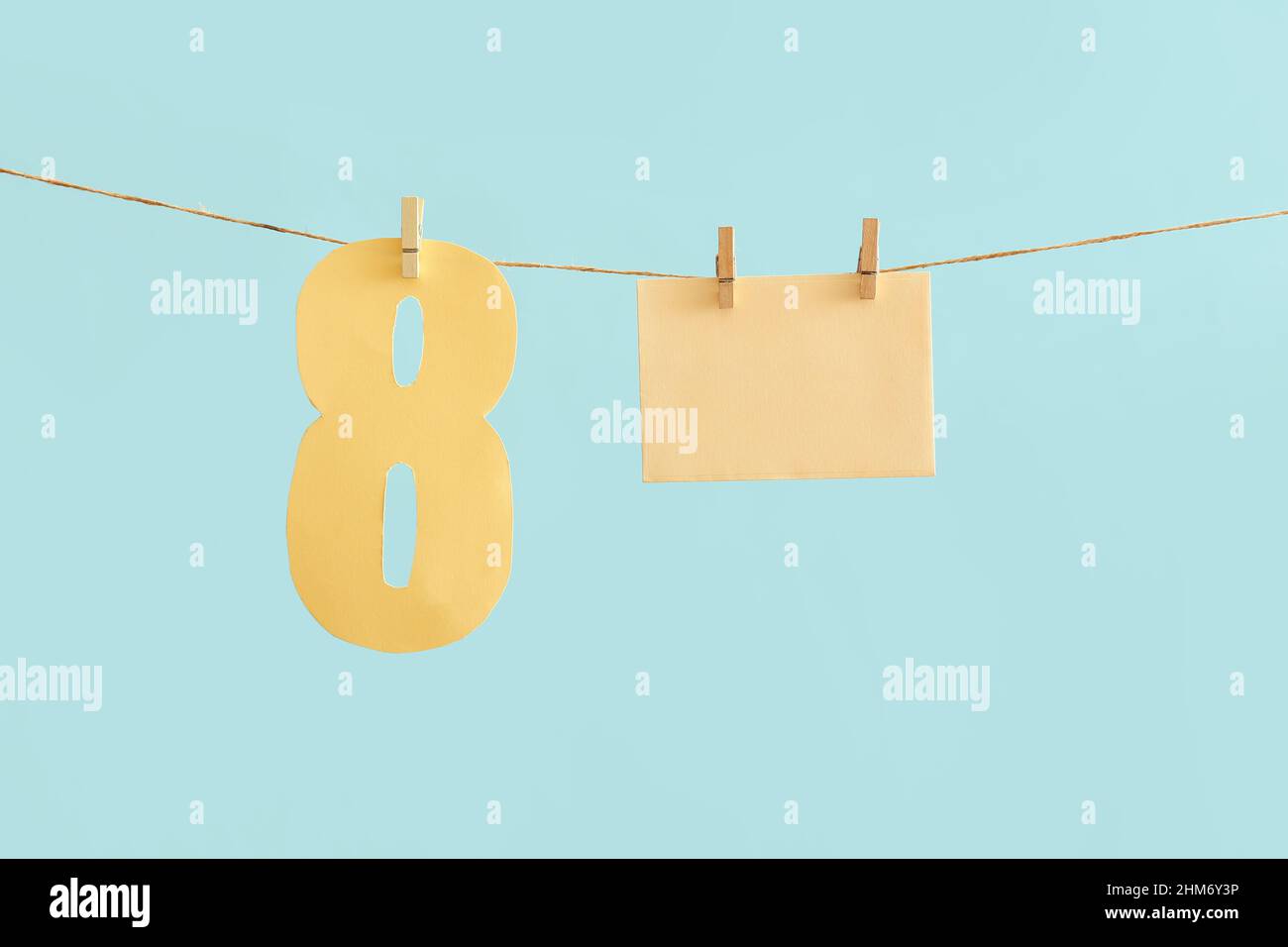Paper figure 8 and blank card hanging on rope against color background ...
