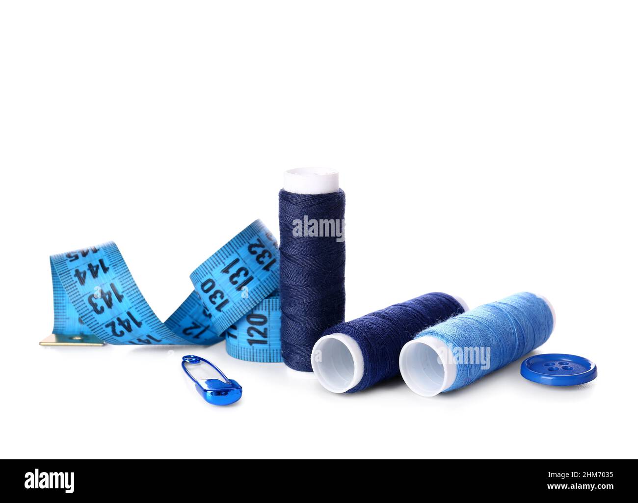 Blue thread spools, button, measuring tape and safety pin on white ...