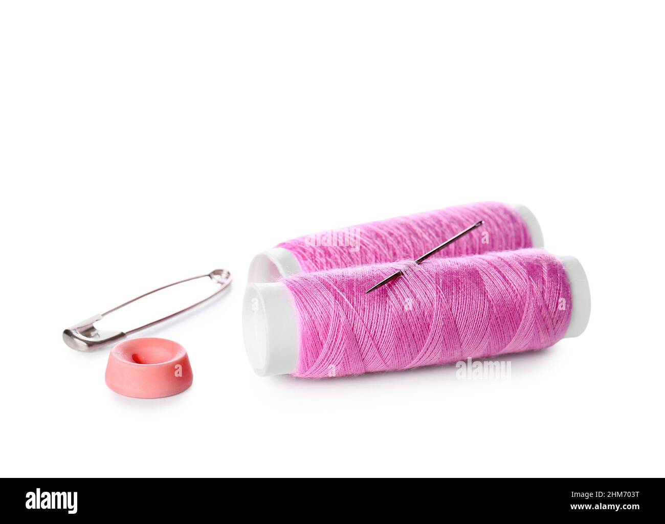 Pink thread spools with needle, button and safety pin on white ...