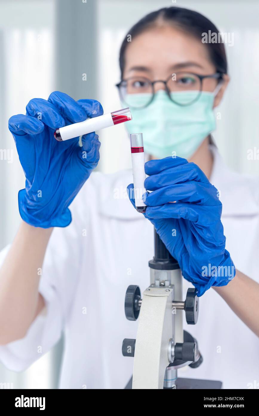 Asian researcher woman with face mask and glasses holding medical tube ...