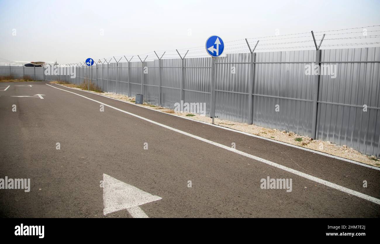 Two straight and left turn arrow signs at the perimeter fencing around ...