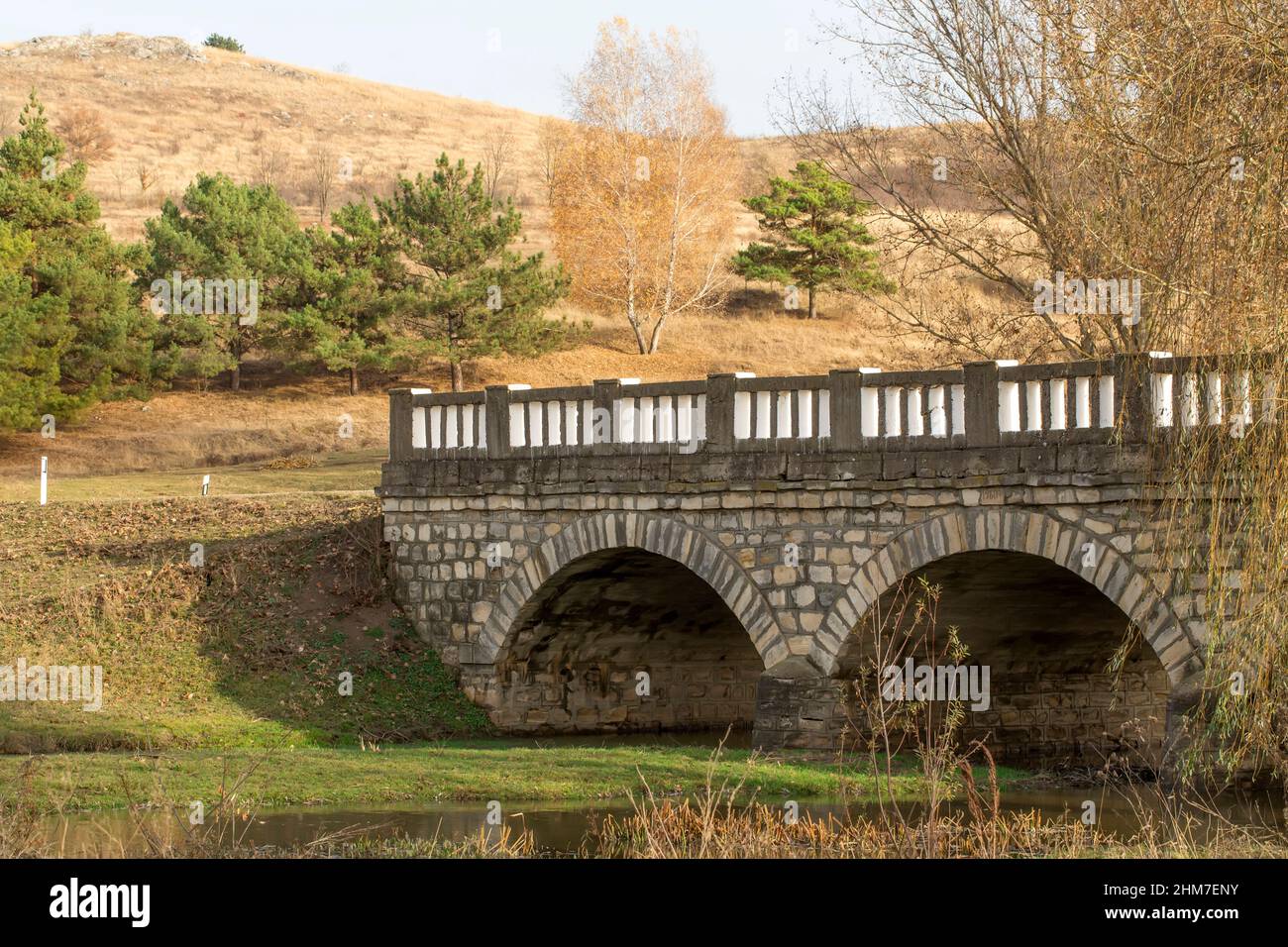 A stone bridge over a small river flowing in country. An autumn ...