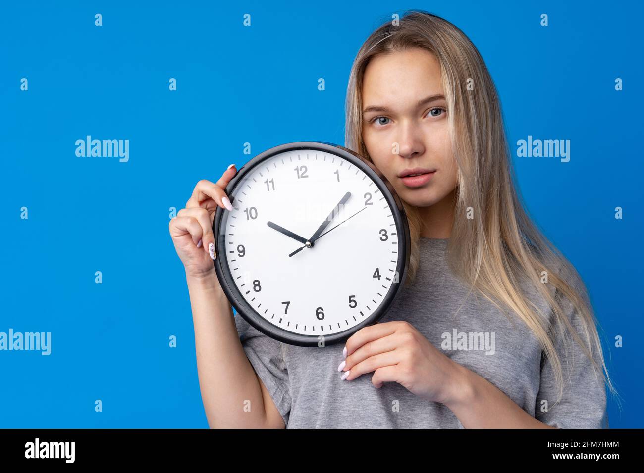 Beautiful teen girl holding wall clock over blue background Stock Photo ...