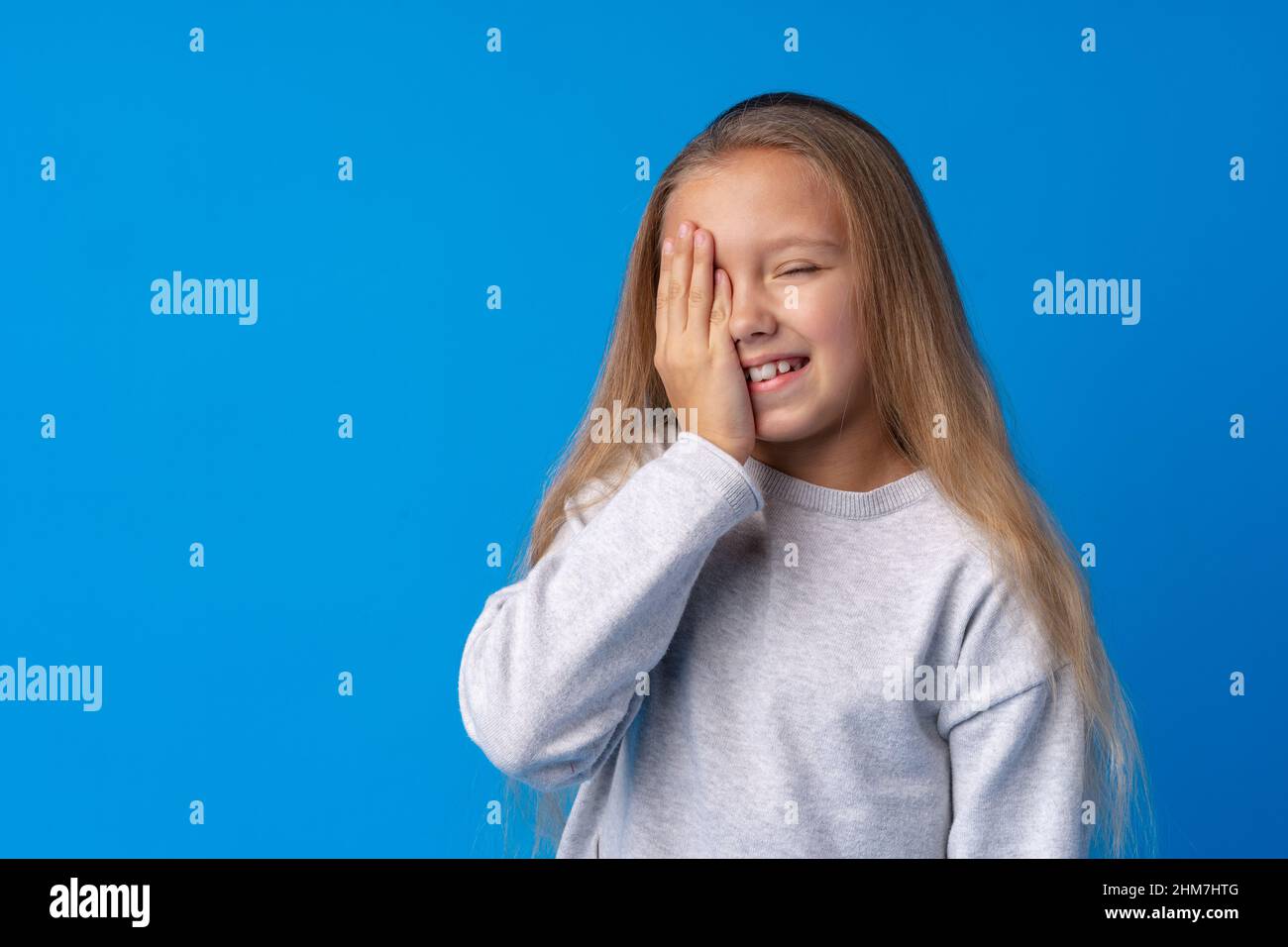 Portrait of cute emotional little girl facepalming on a blue background ...