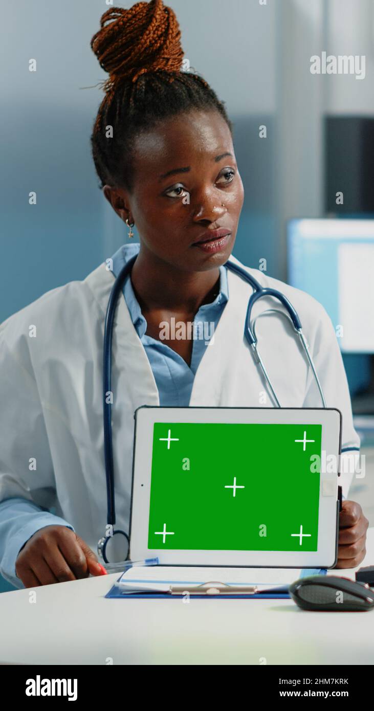Black doctor showing tablet with horizontal green screen to patient at ...