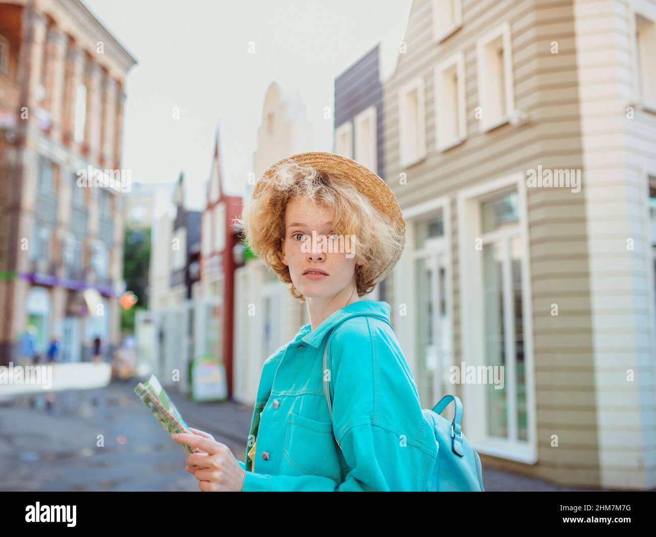 Portrait of redhead young woman in straw hat and with travel bag with ...
