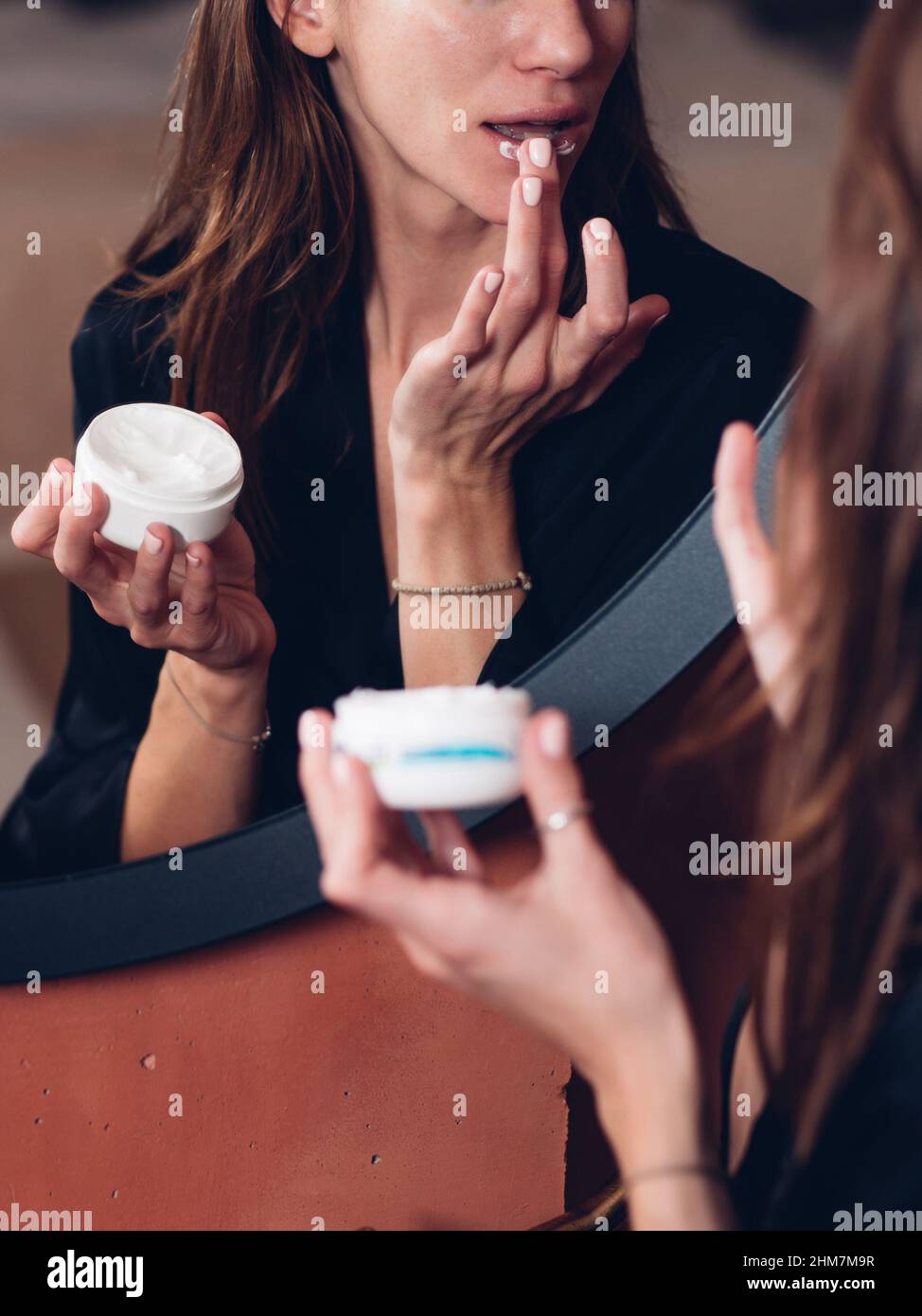 Woman applies a nourishing balm to her lips, moisturizing her skin ...