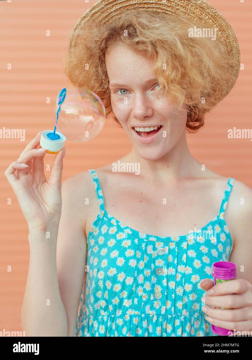 young cheerful curly redhead woman in blue sundress and straw hat with ...