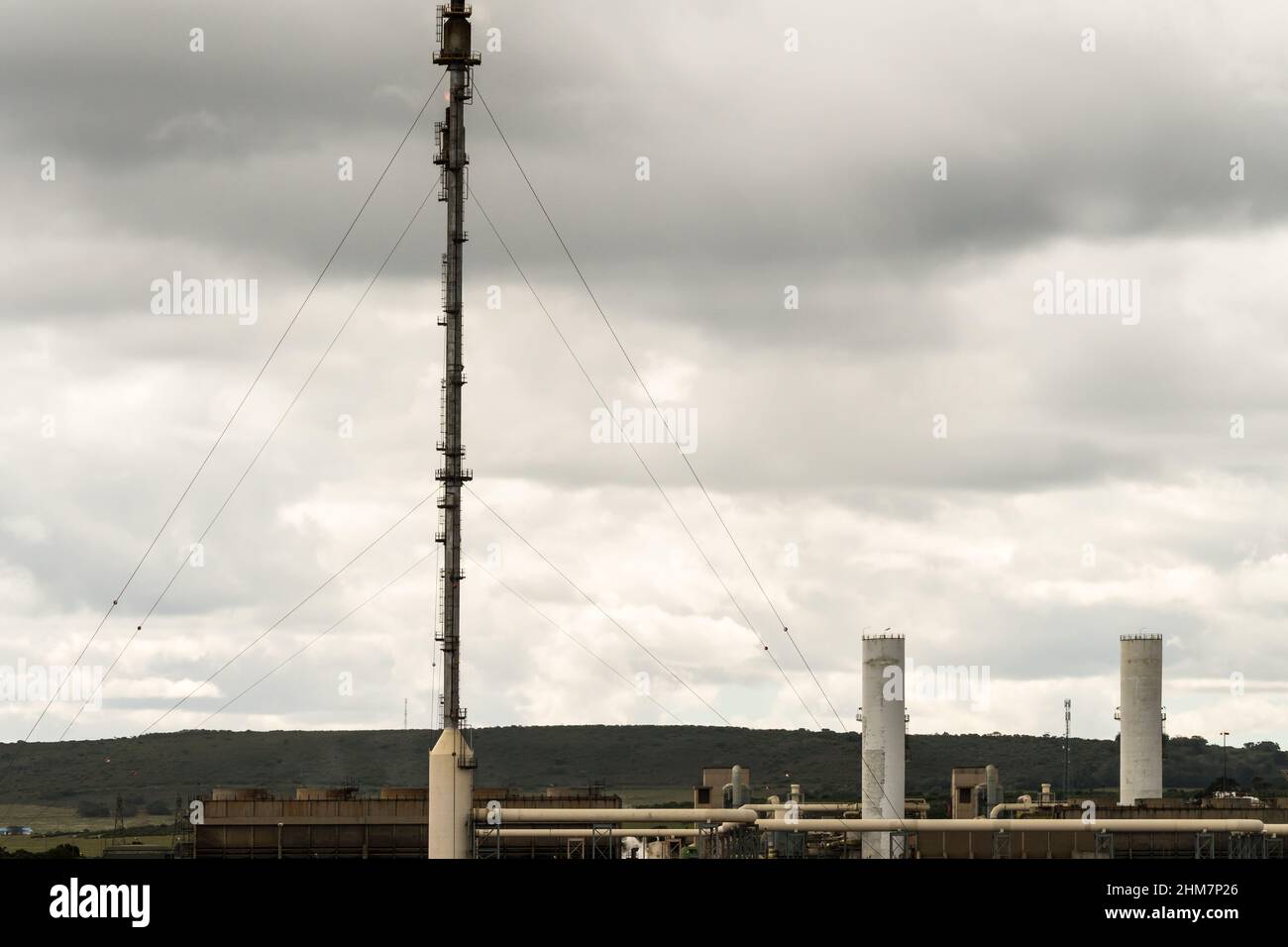 refinery metal chimney with flame close up against grey clouds in ...