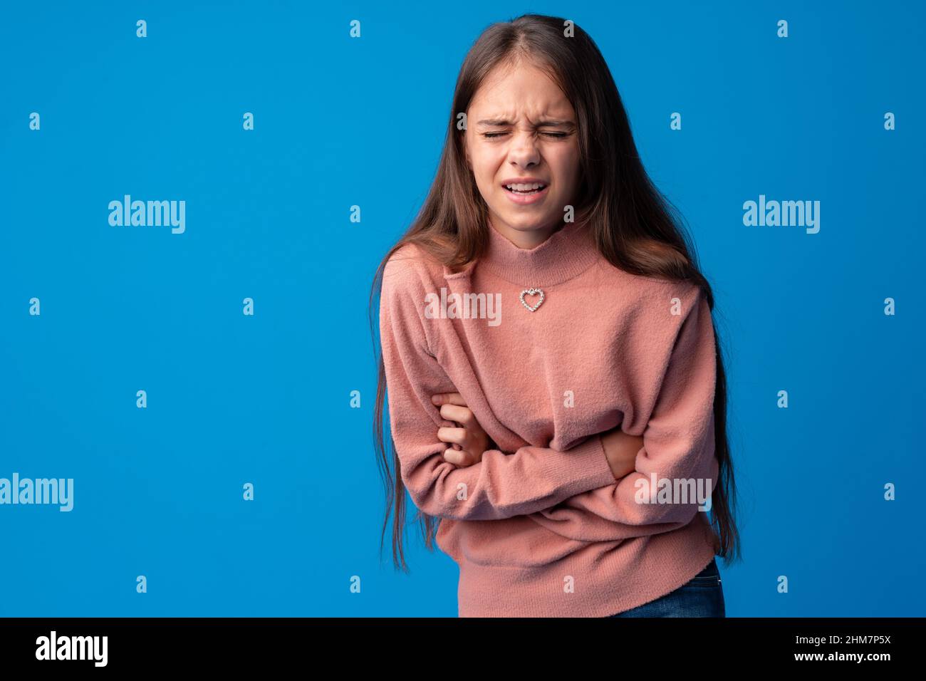Young girl with bellyache isolated on a blue background Stock Photo - Alamy