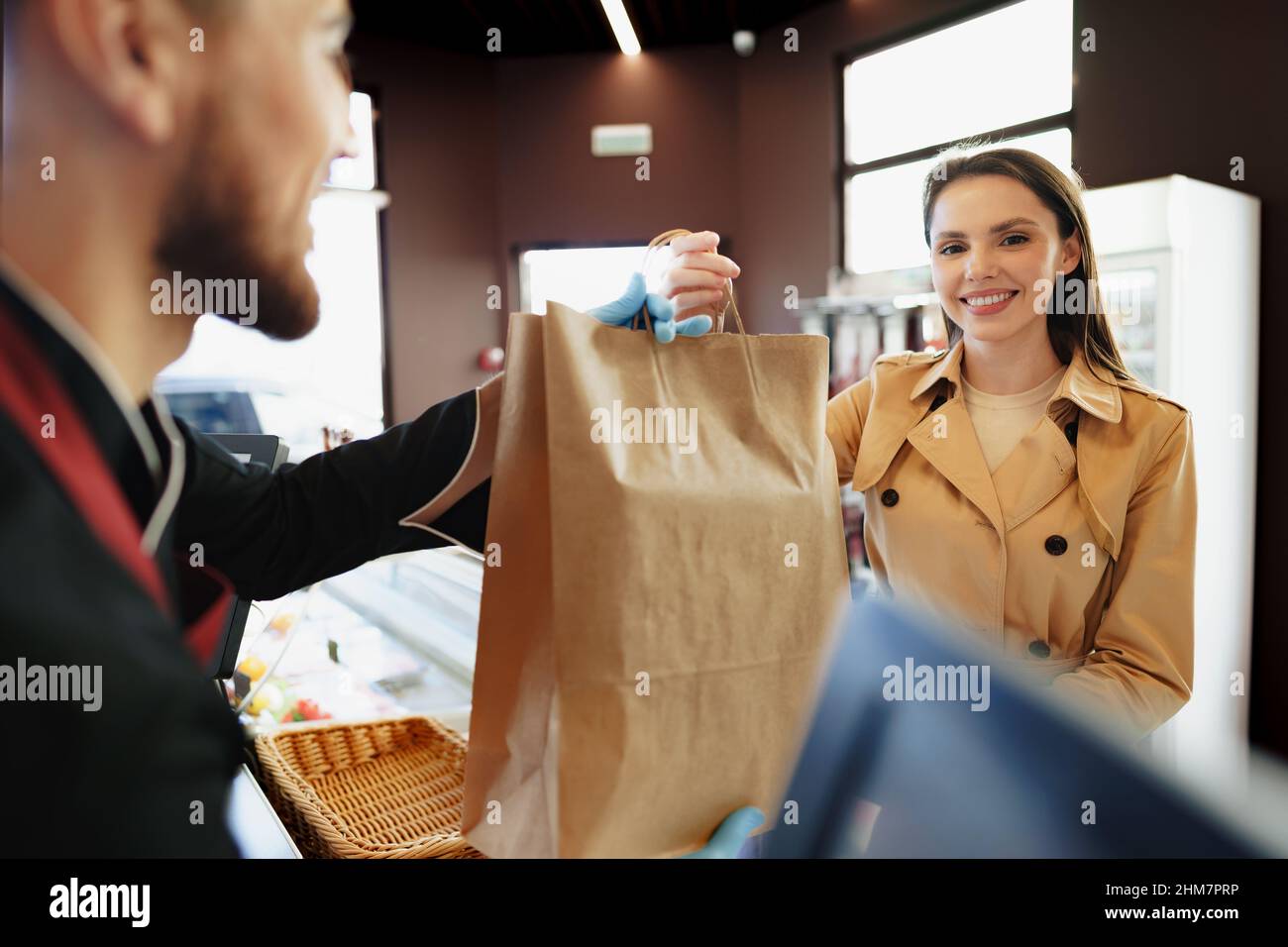 Shop assistant handling shopping bag to female customer in grocery ...