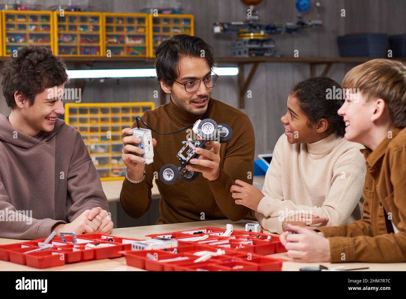 Portrait of young teacher helping diverse group of kids building robots ...
