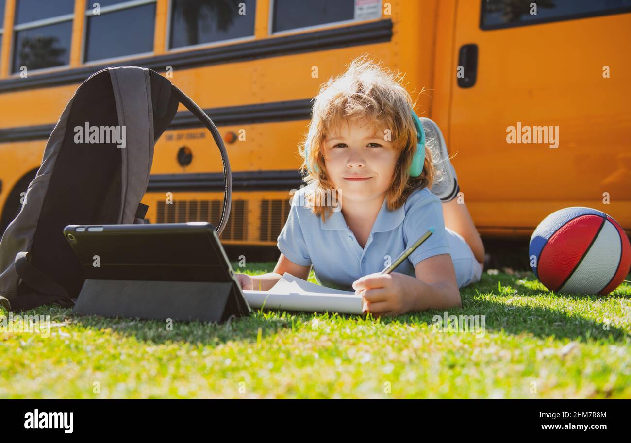 Pupil writing homework on grass with laptop tablet outdoor near school ...