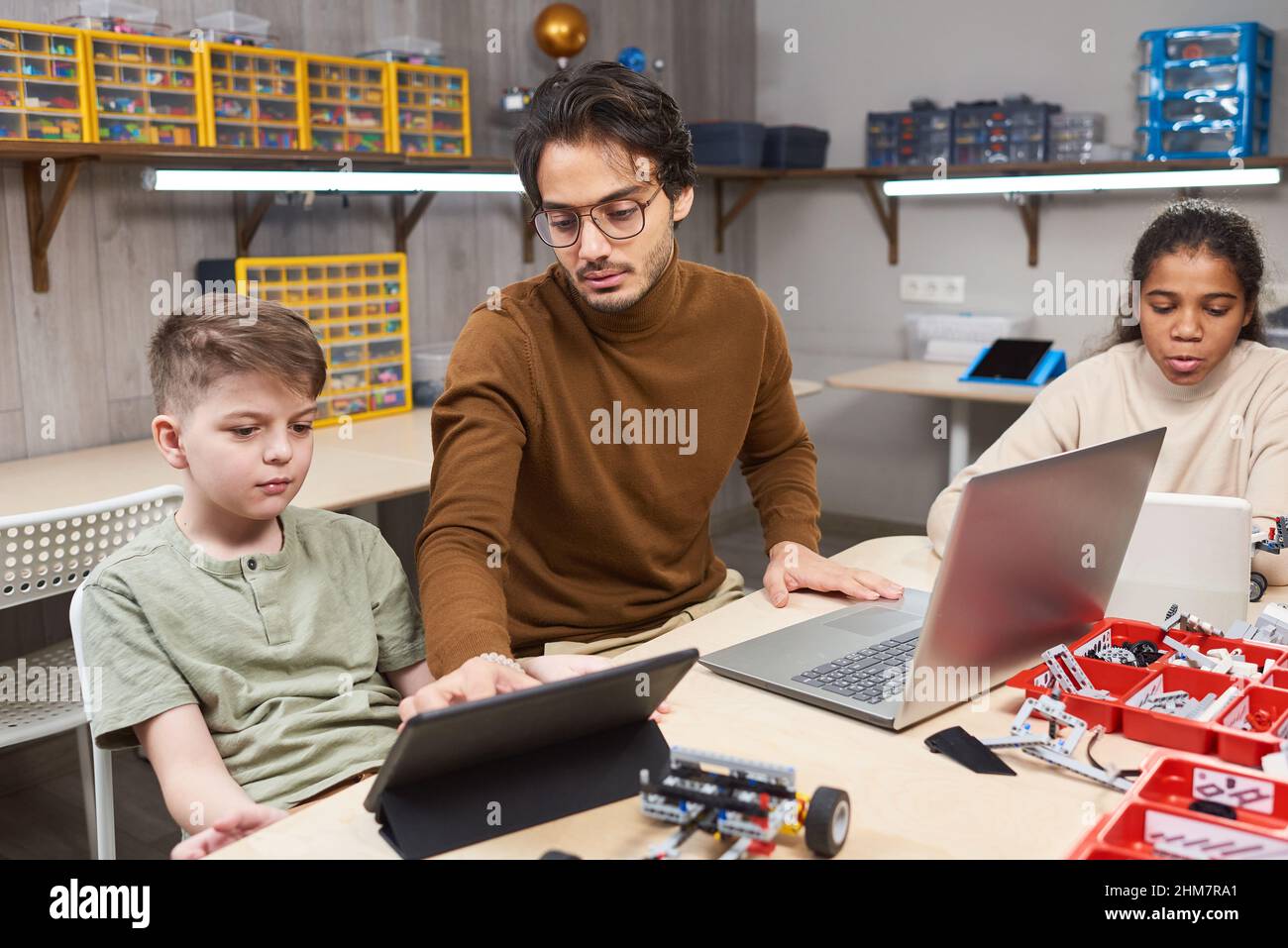 Portrait of young man teaching robotics class to diverse group of ...